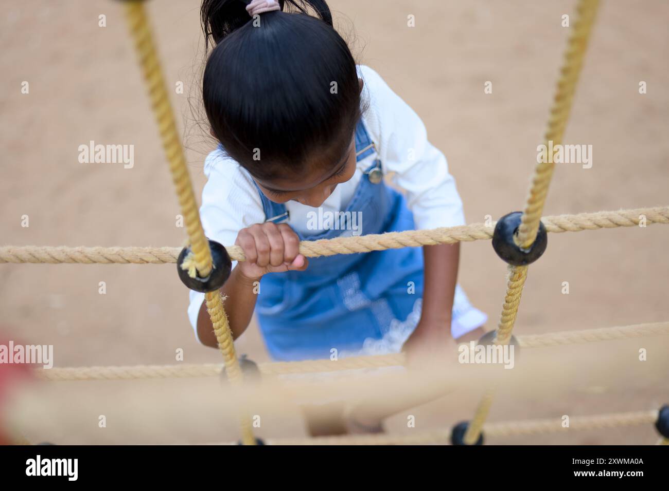 Determined young girl navigating a rope obstacle course, focused on ...