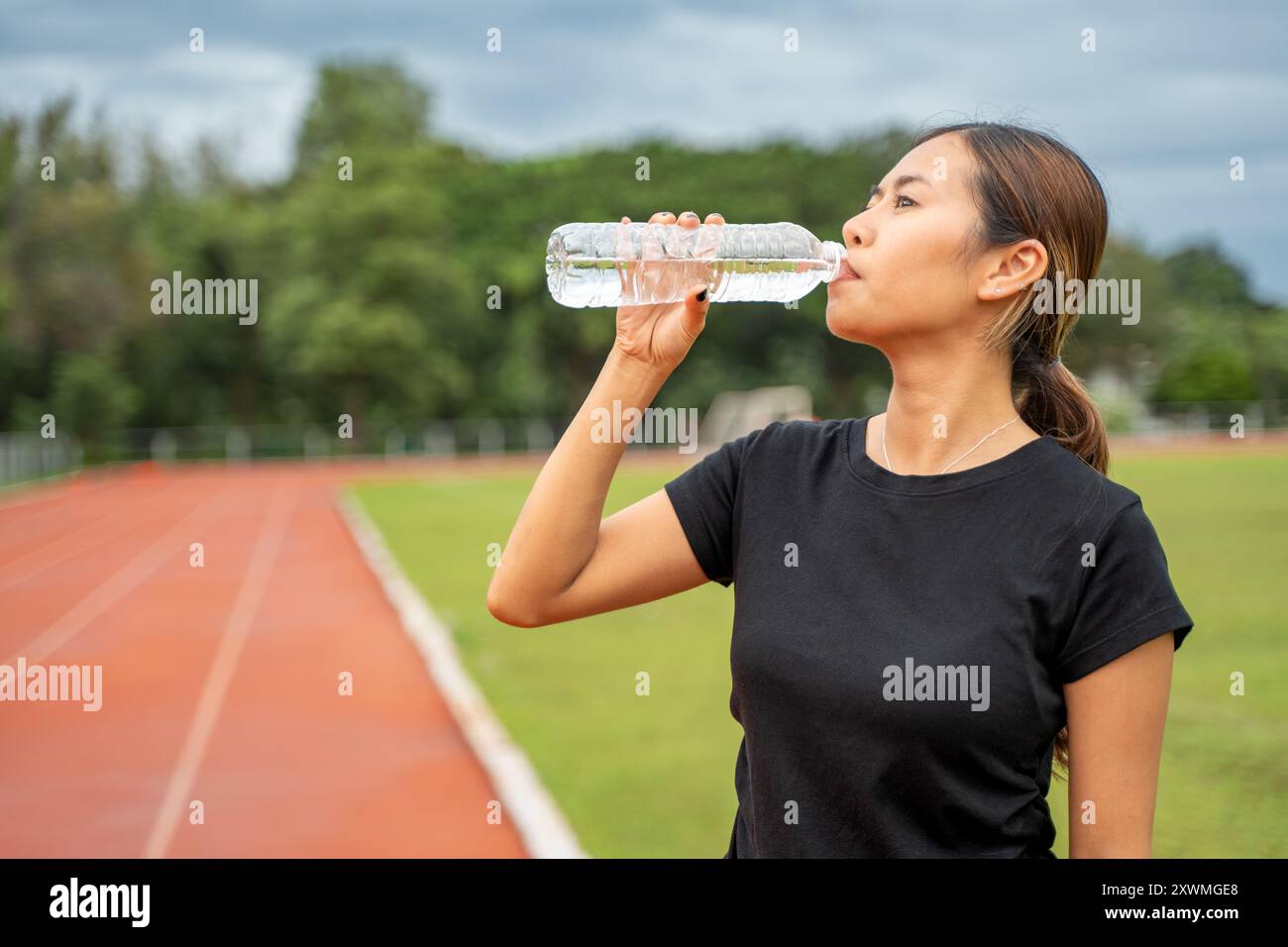 Tired young female runner drinking water from a plastic bottle during ...