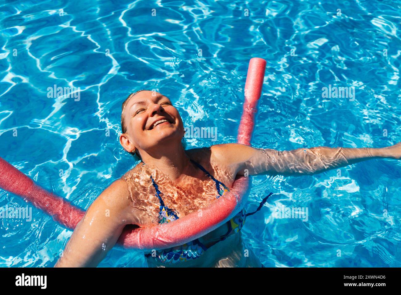 A senior woman enjoys a sunny day floating in a pool using a pink ...