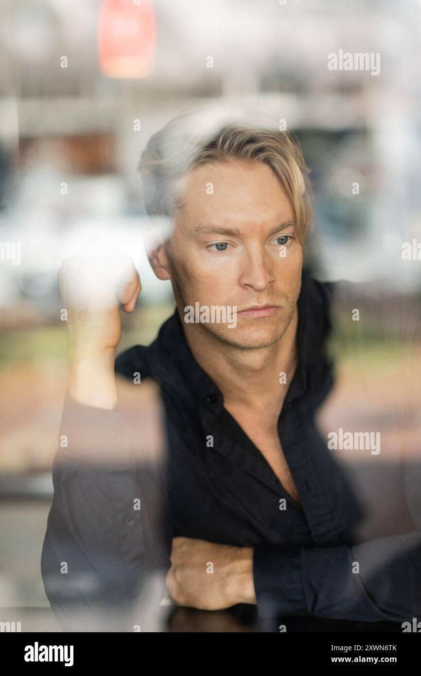 A handsome blonde man in a stylish black shirt gazes thoughtfully out a ...