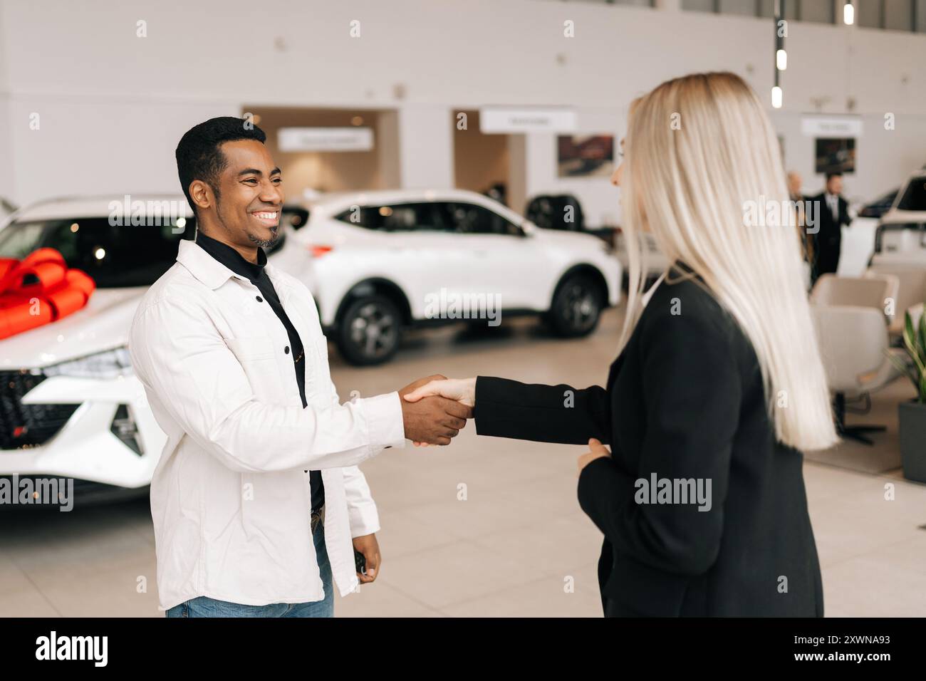 Happy cheerful female dealer and African-American customer male shaking ...