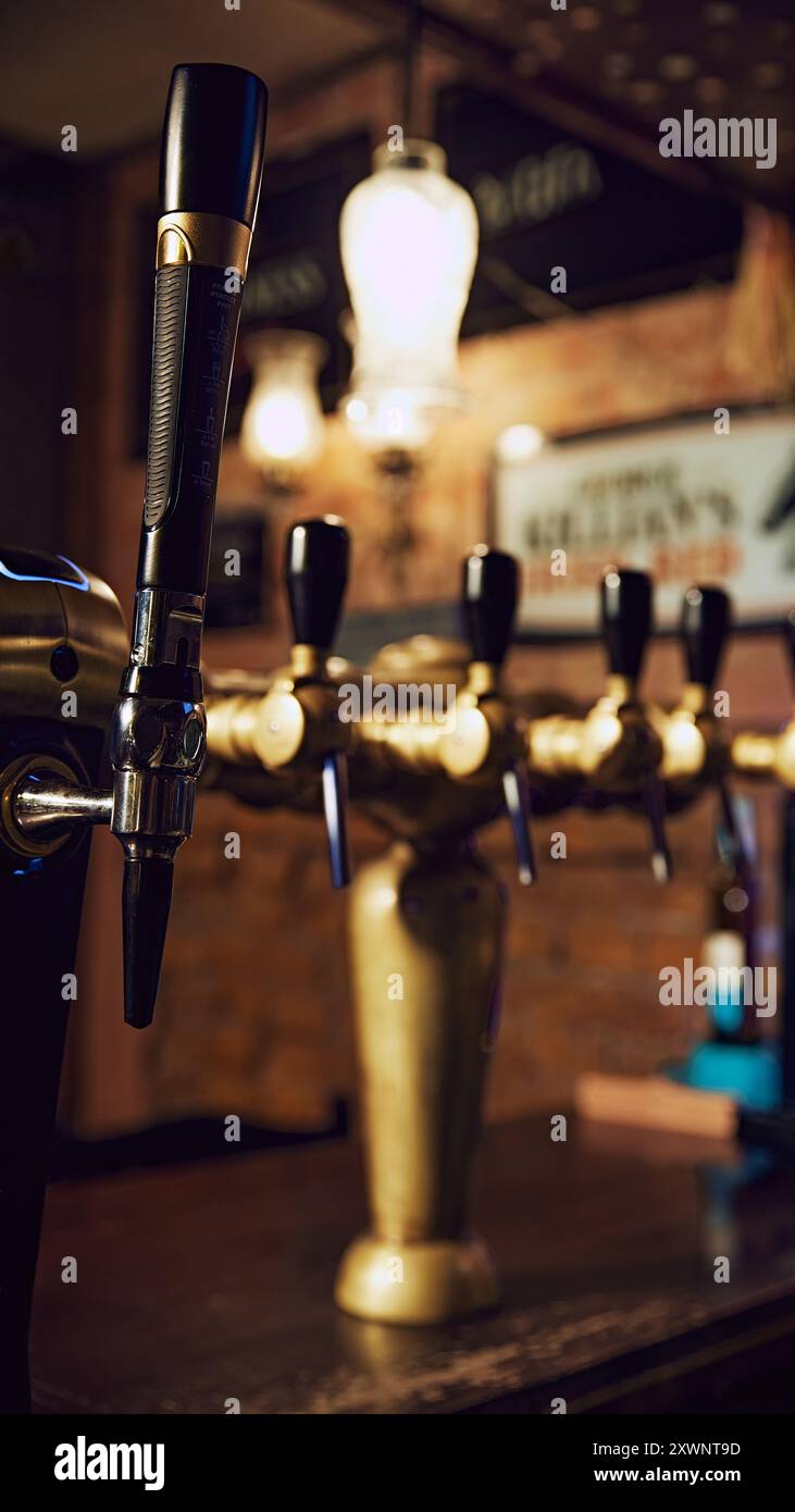 Close-up of row of shiny brass beer taps with handles, set against dark ...