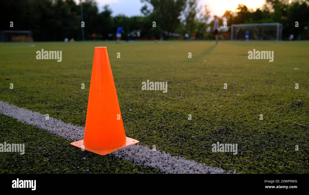 Orange training cone on soccer field at sunset. Football practice equipment on grass with goal ...