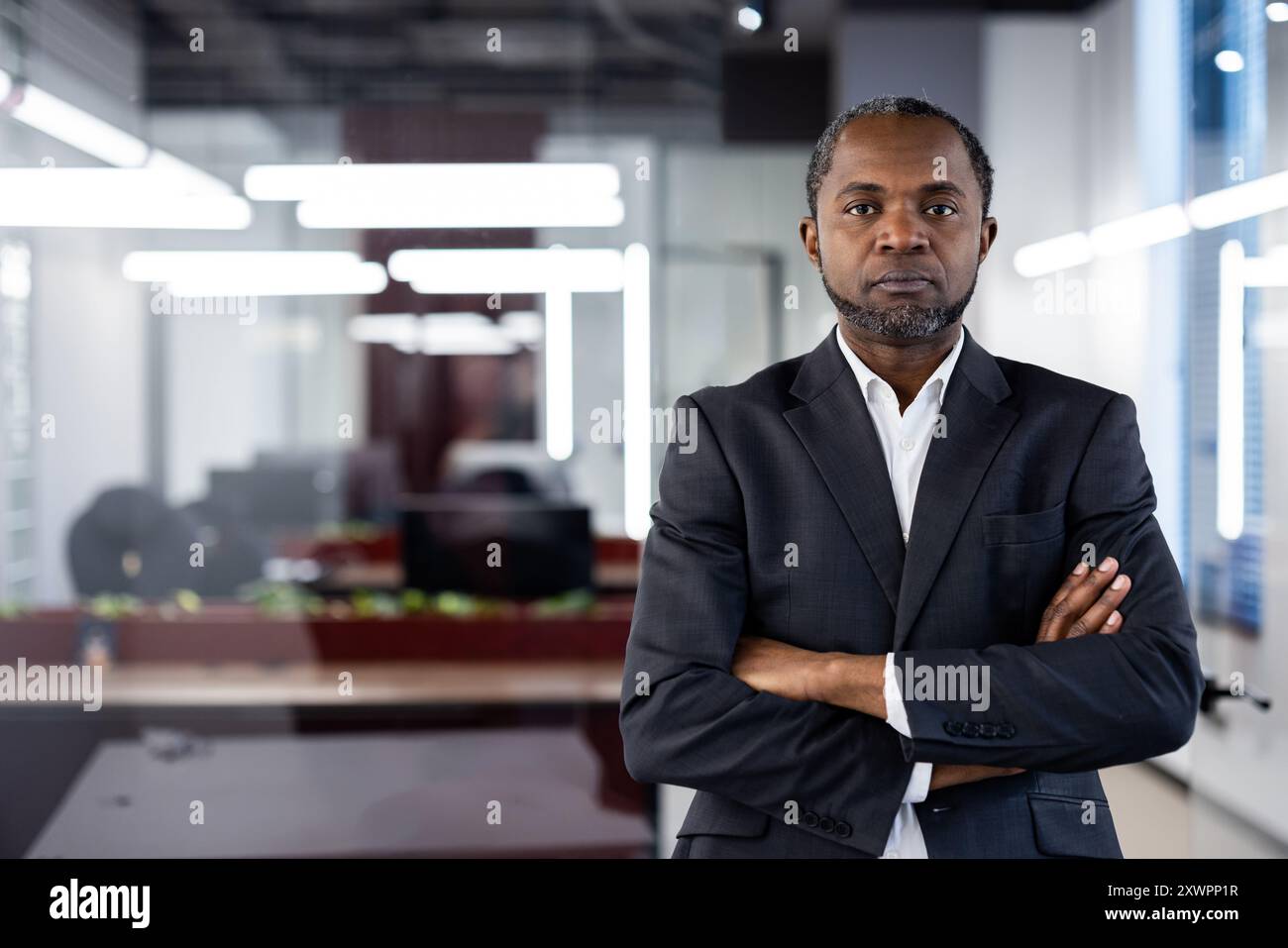 Confident businessman standing with arms crossed in modern office ...
