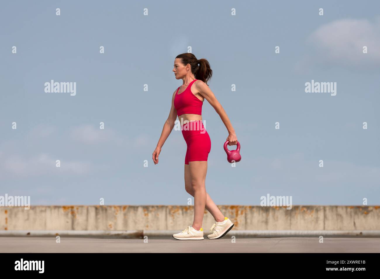 Sporty mid adult woman carrying a kettlebell weight, training outdoors ...