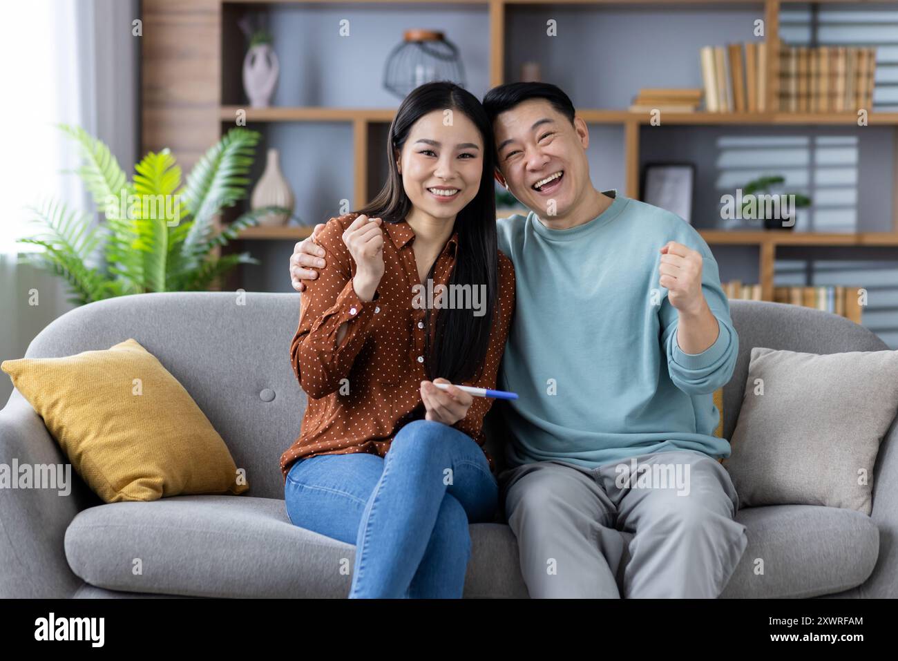 Joyful Asian Couple Celebrating Positive Pregnancy Test Result On Sofa 6653