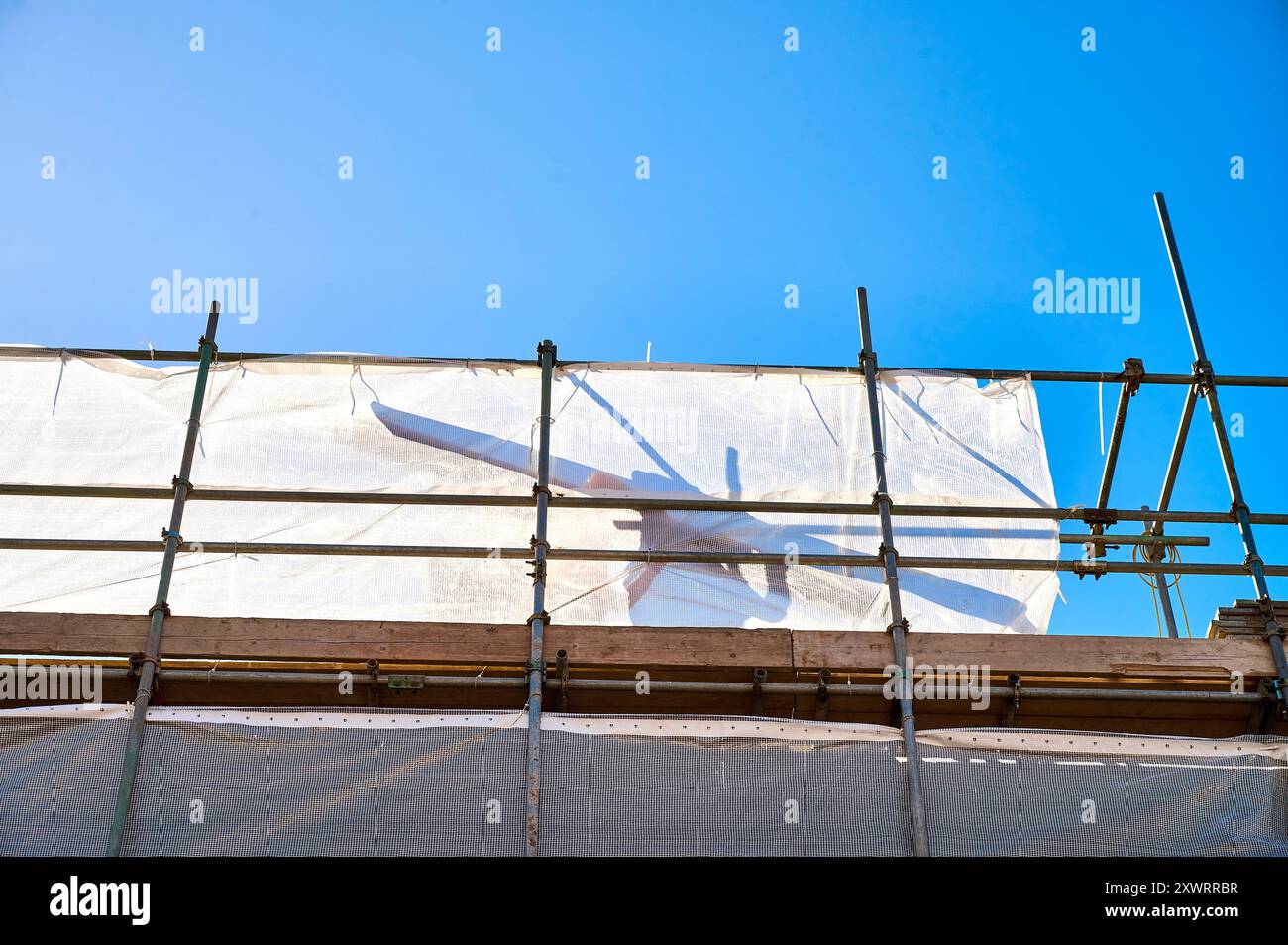 Shadow of builder behind plastic sheet carrying a plank at top of ...