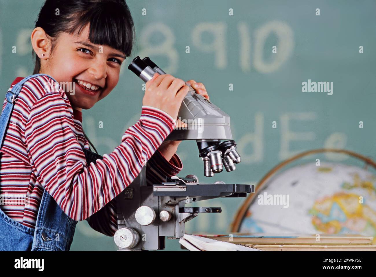 A Portrait of a smiling girl examines samples through a microscope in a ...