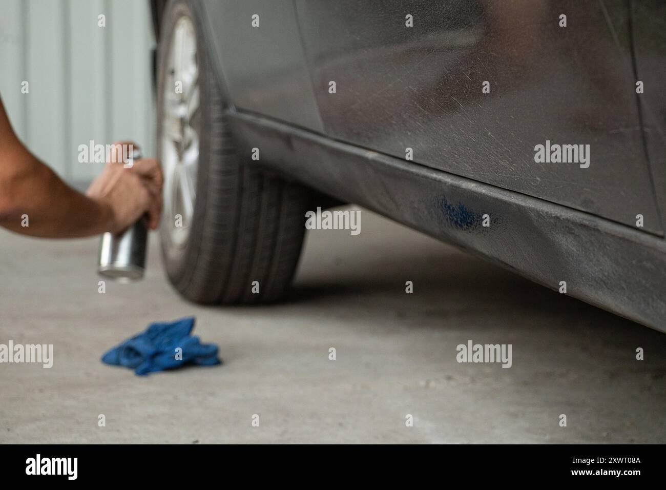 A man spray paints a car in a yard with black paint, hiding the rust on ...