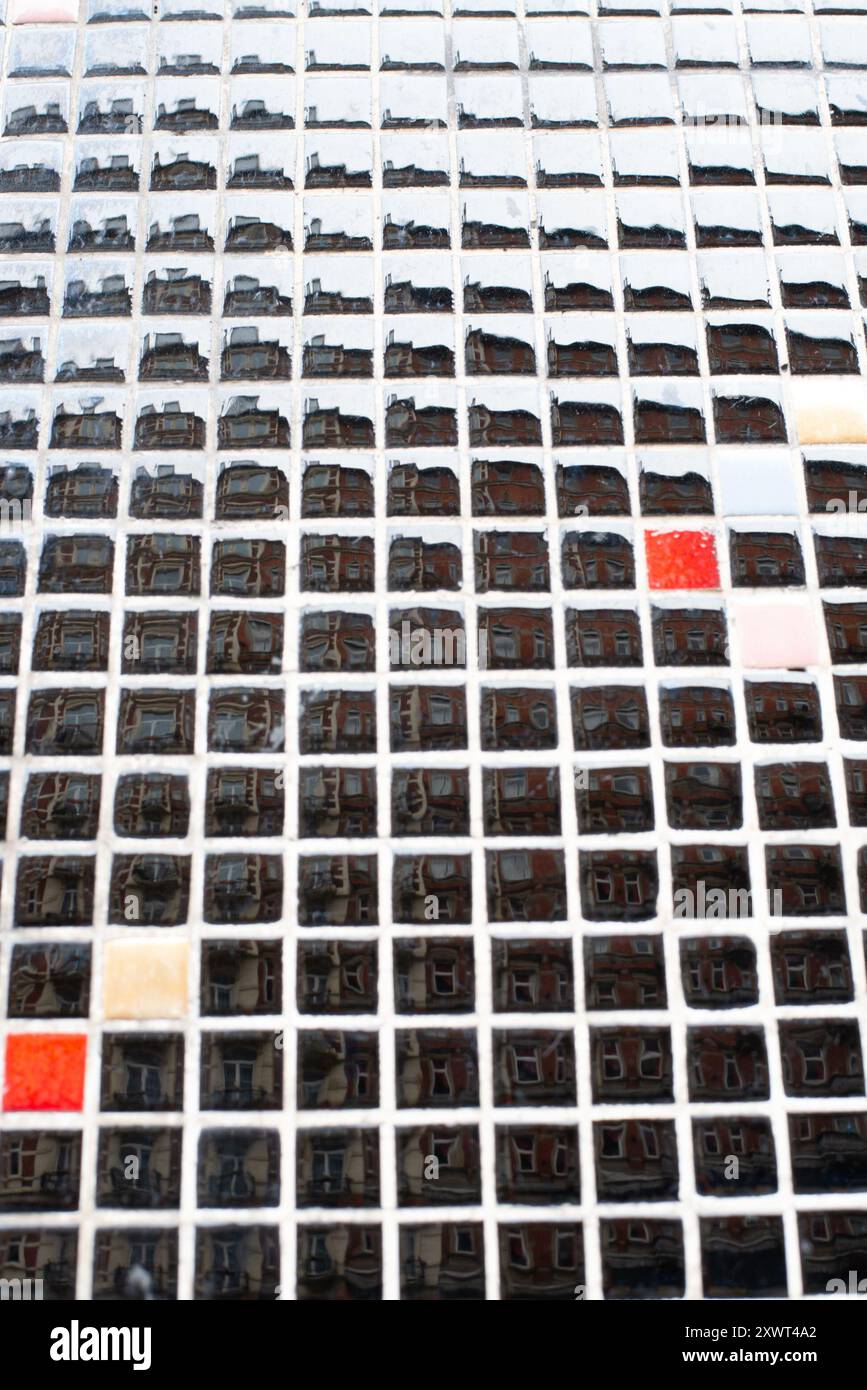 The photo captures the reflection of buildings on a grid of glass tiles ...