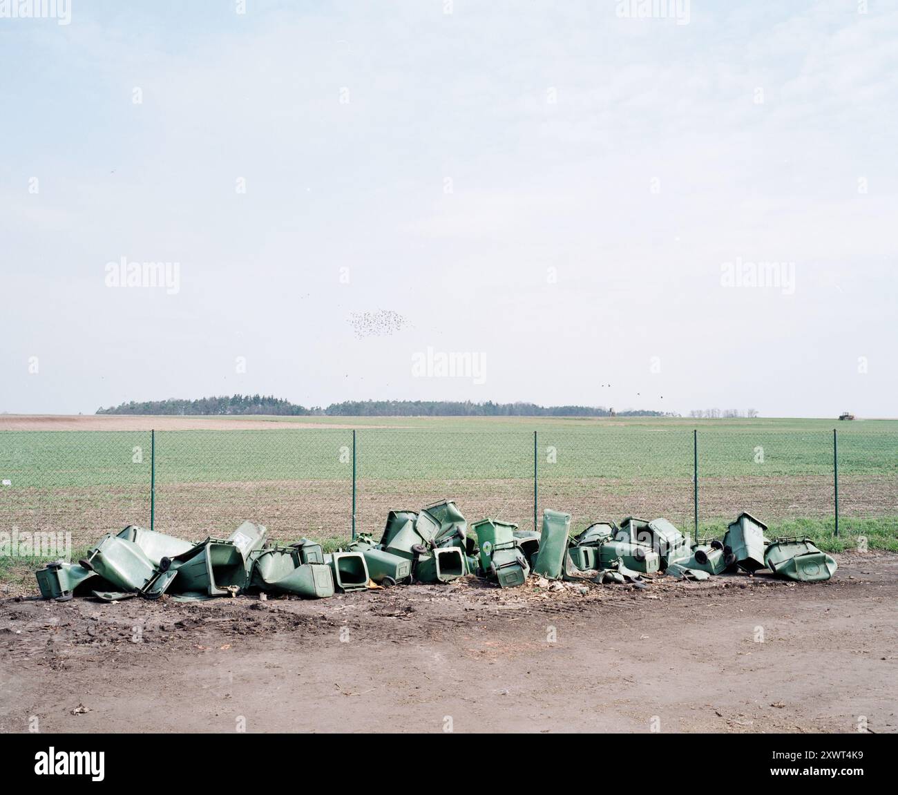Pile of green garbage bins dumped by the side of an open field. The ...