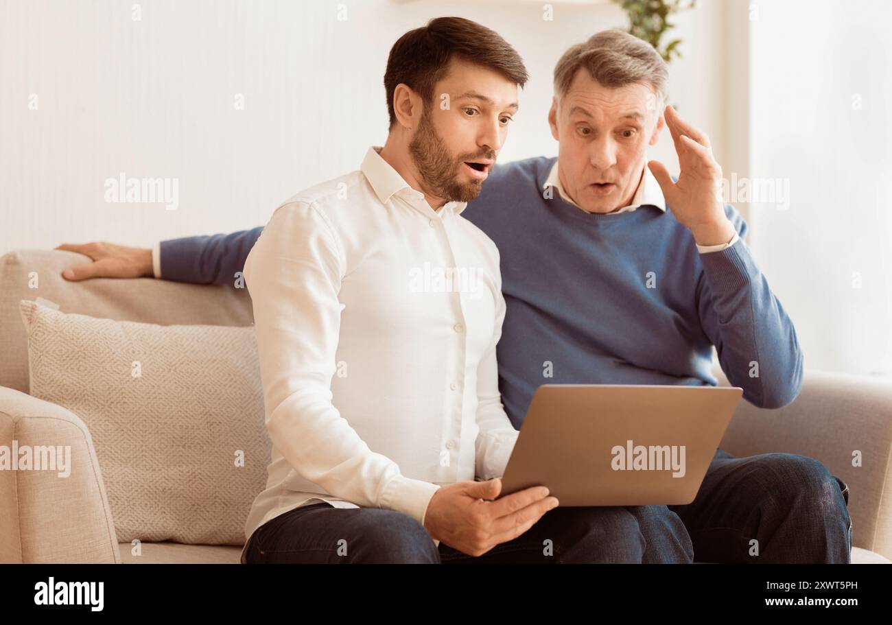 Shocked elderly man and adult son using laptop sitting indoor Stock ...