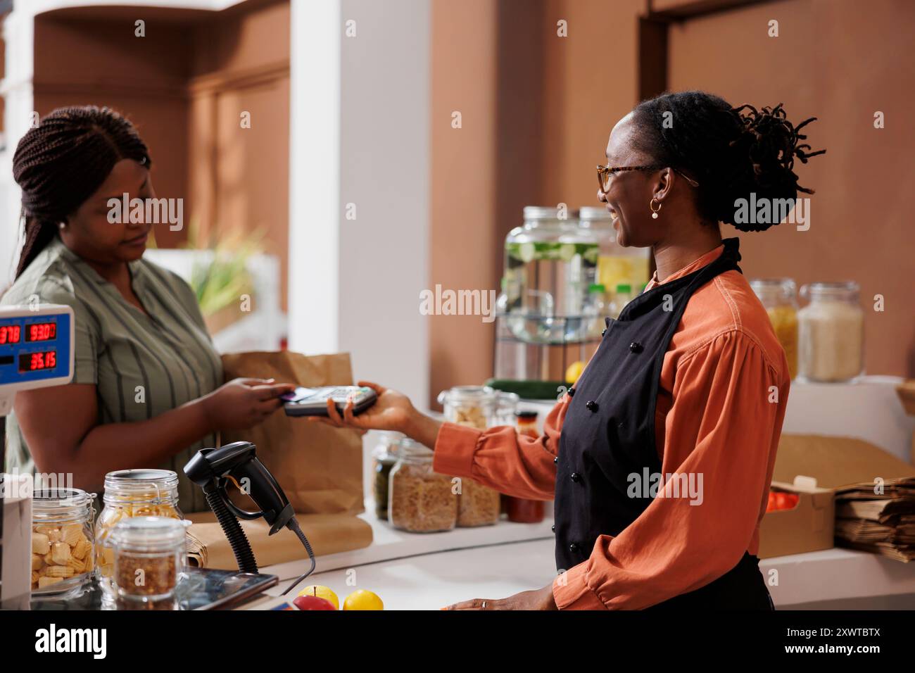 African American woman happily makes cashless payment at market counter ...