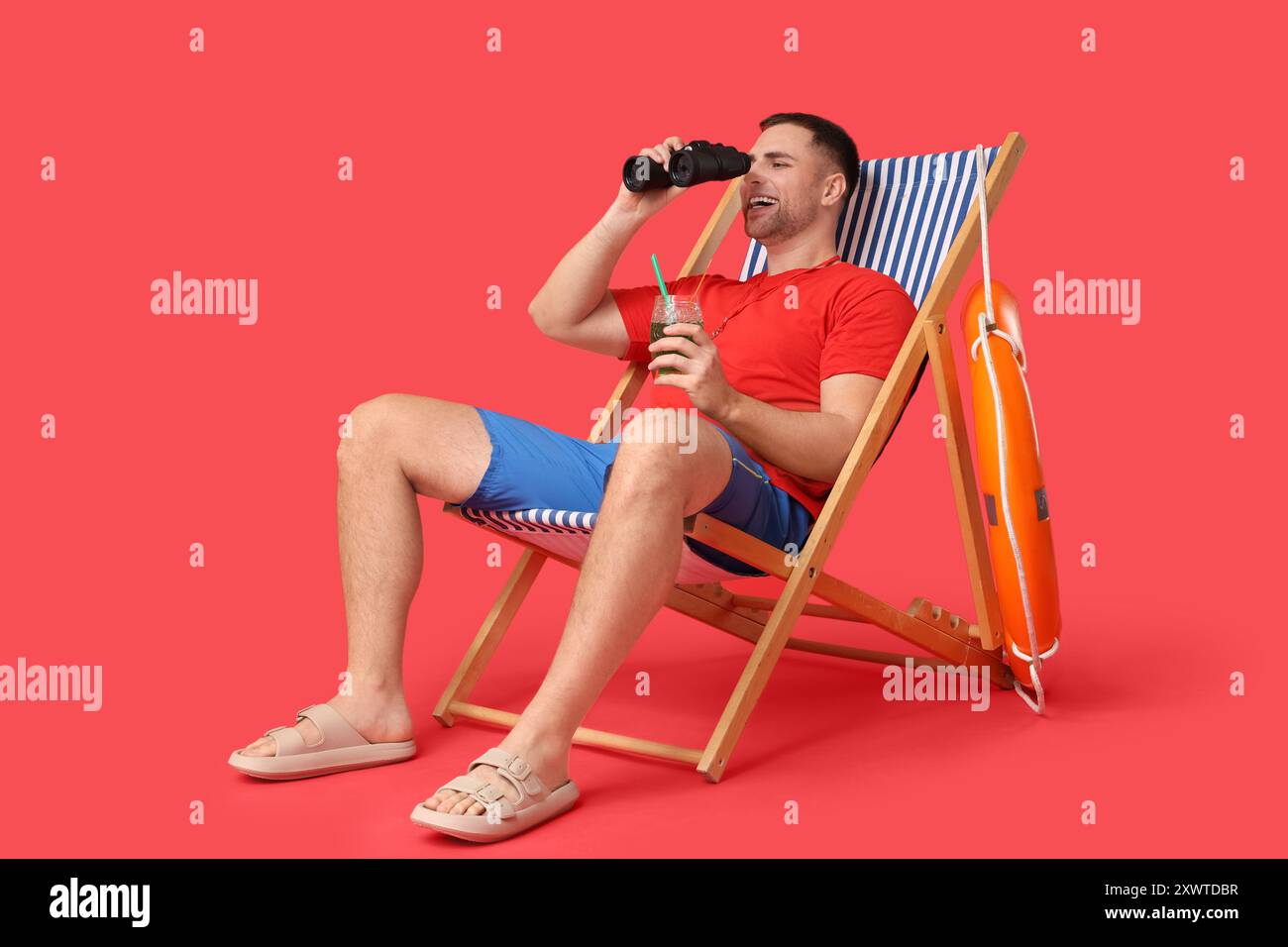 Happy young lifeguard with cocktail, lifebuoy and binoculars sitting on ...