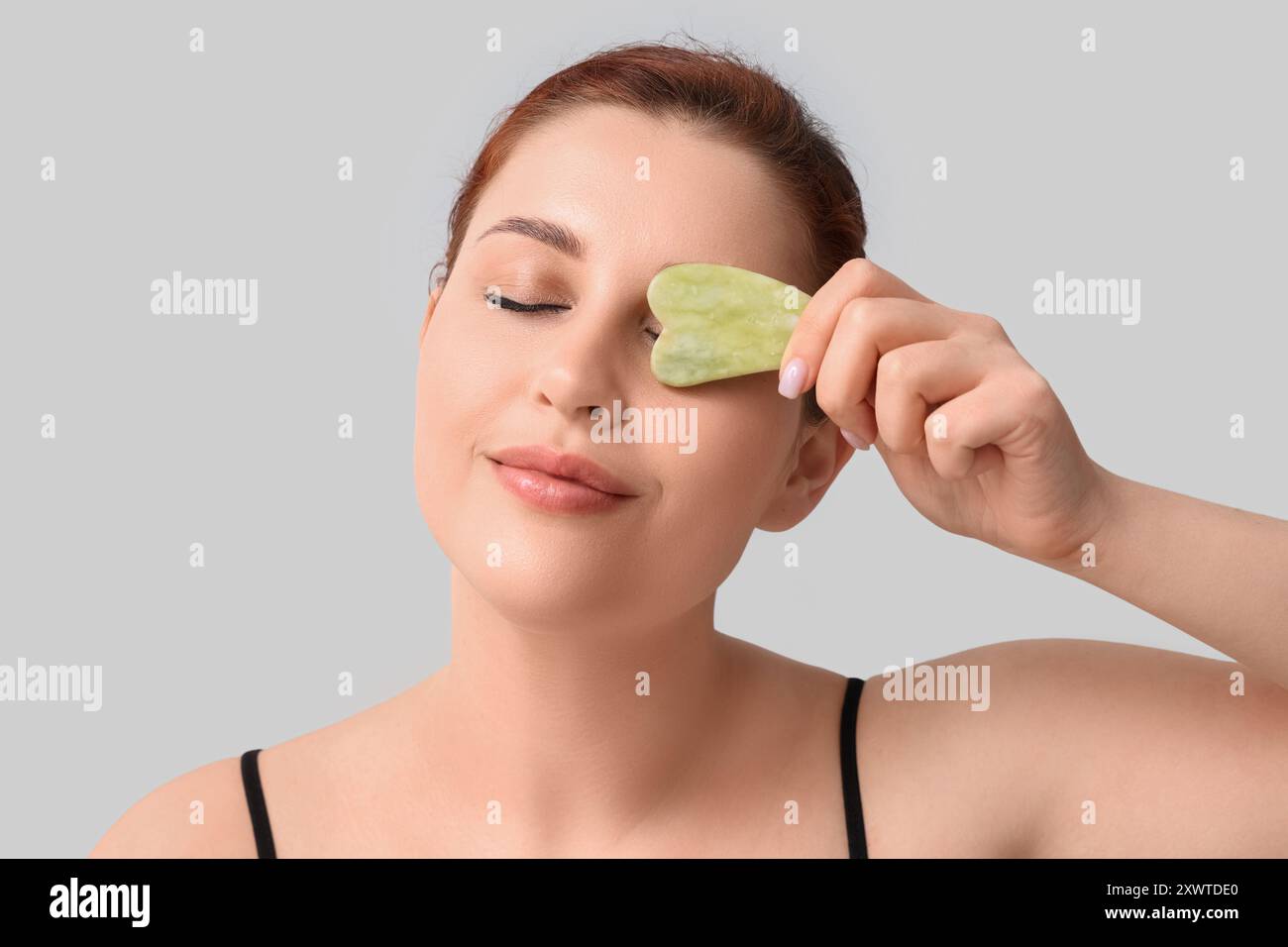 Beautiful young woman covering one eye by guasha tool on grey ...