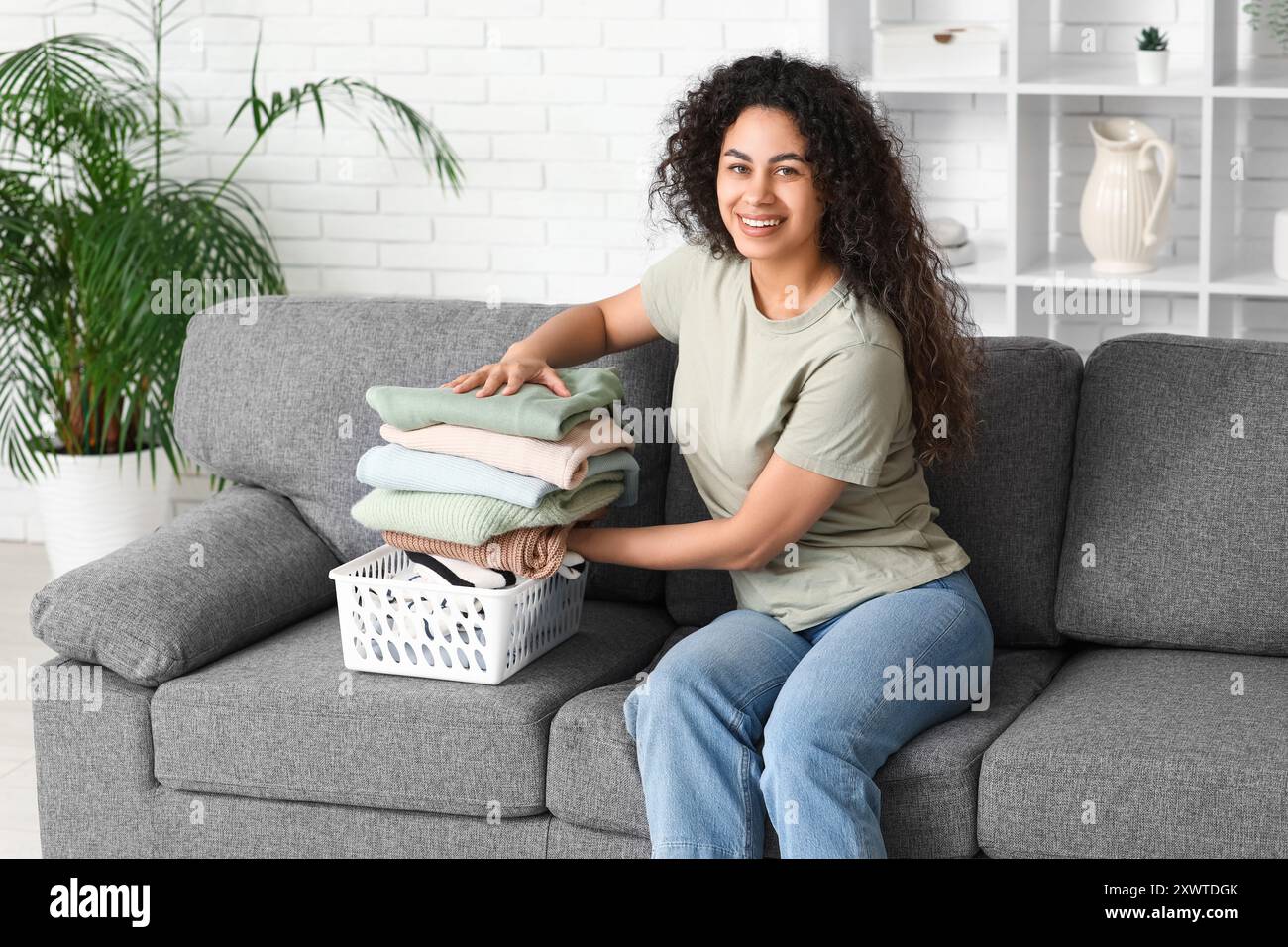 Beautiful young happy African-American woman folding clean clothes at ...