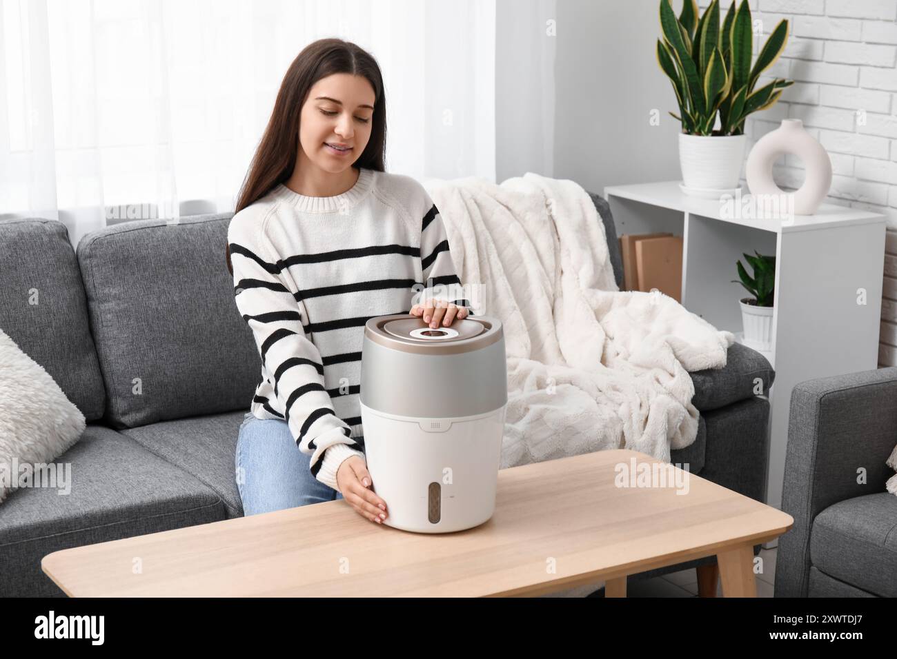 Young woman sitting on black sofa and turning on modern humidifier in ...