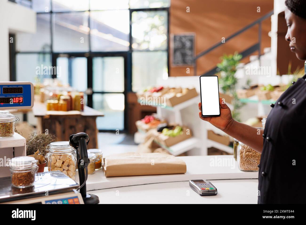 Storeworker, in black apron, glances at mobile device with blank mockup ...