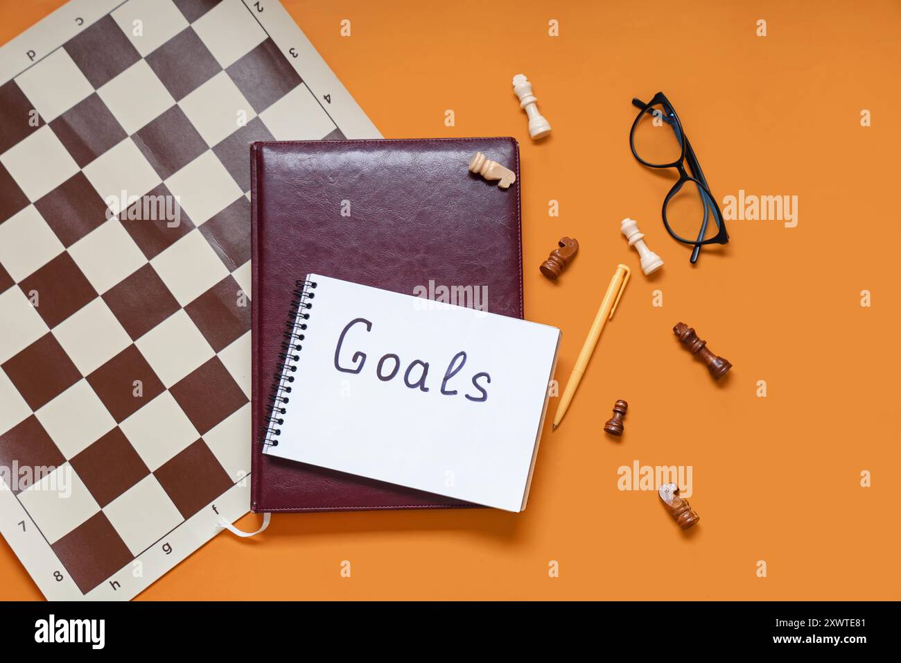 Chess pieces, game board and notebook with text GOALS on orange ...