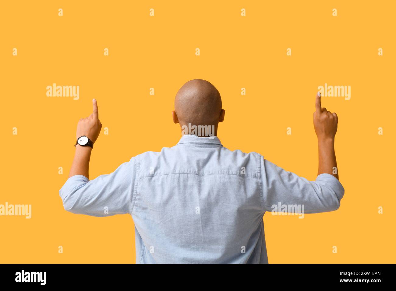 Bald young man pointing at something on yellow background, back view ...