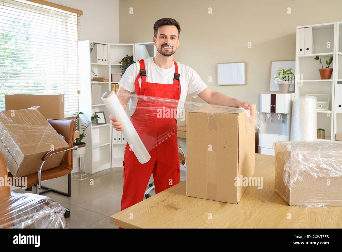 Male worker wrapping box with stretch film in office Stock Photo - Alamy