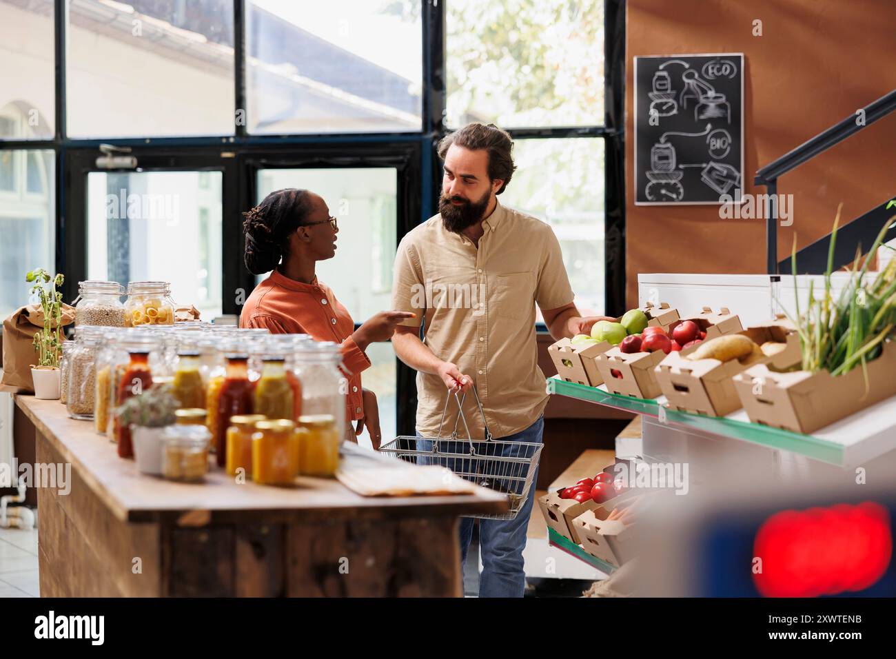 Vegan multiracial couple carrying a basket in a specialty zero waste supermarket buying locally ...