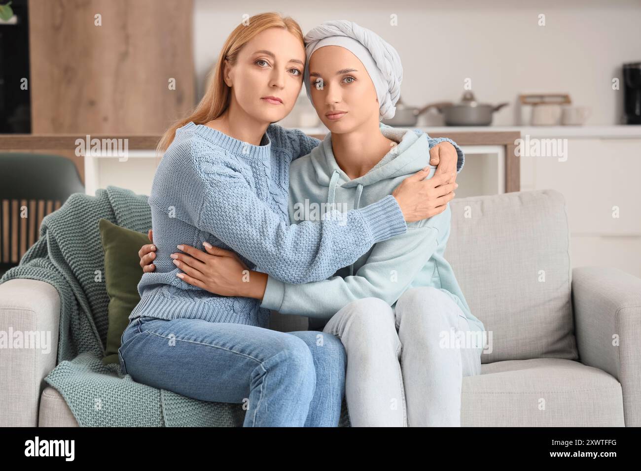 Young woman after chemotherapy with her mother hugging on sofa at home ...