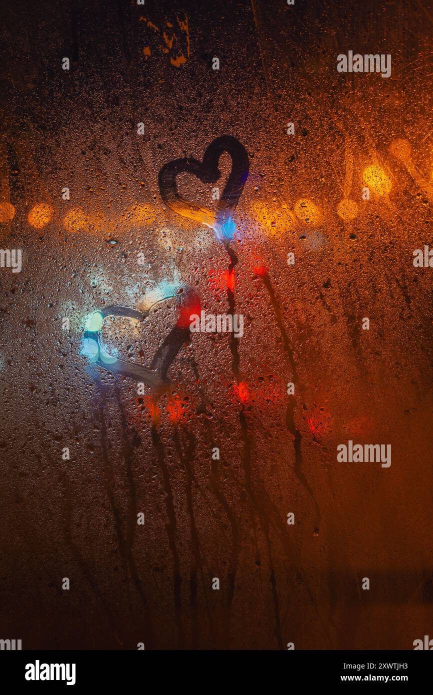 Heart drawn on a foggy window with colorful lights in the background ...
