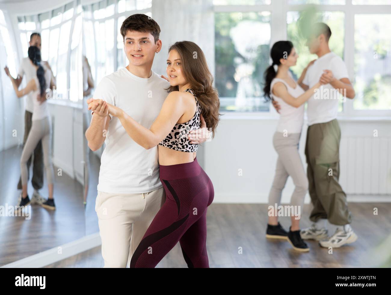 Pretty young woman dancing waltz with partner at group of multinational ...