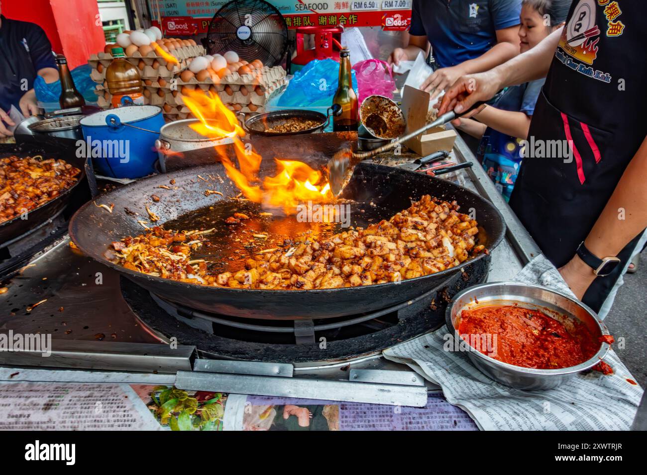 A man cooking street food in a large pan with flames coming from the ...