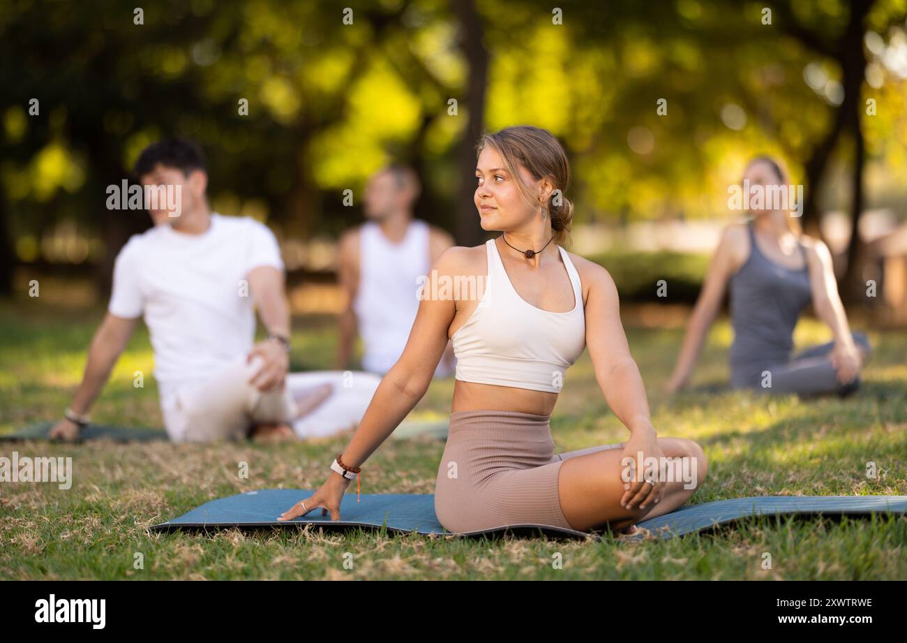 Girl performing stretches in lotus position during group yoga outdoors ...