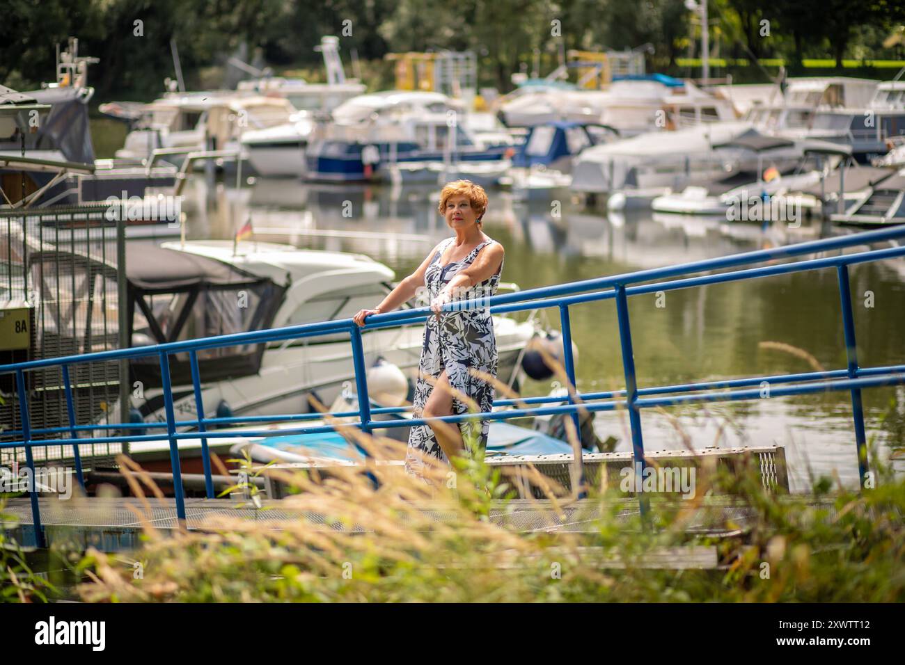 A woman poses on a blue ramp beside a marina with various boats under a ...