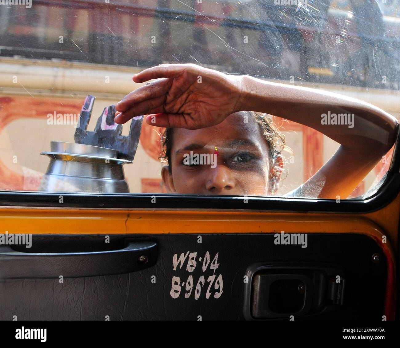 A young beggar knocking on window and taxis on a busy street in Kolkata ...