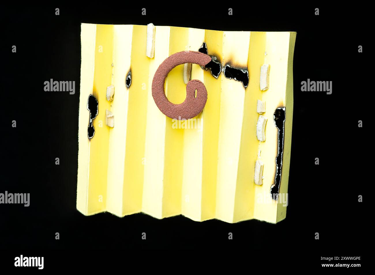 A yellow piece of paper with a mosquito coils on it. A brown object is ...