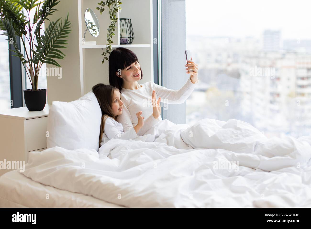 Mom and daughter lying in bed having video call on phone Stock Photo ...