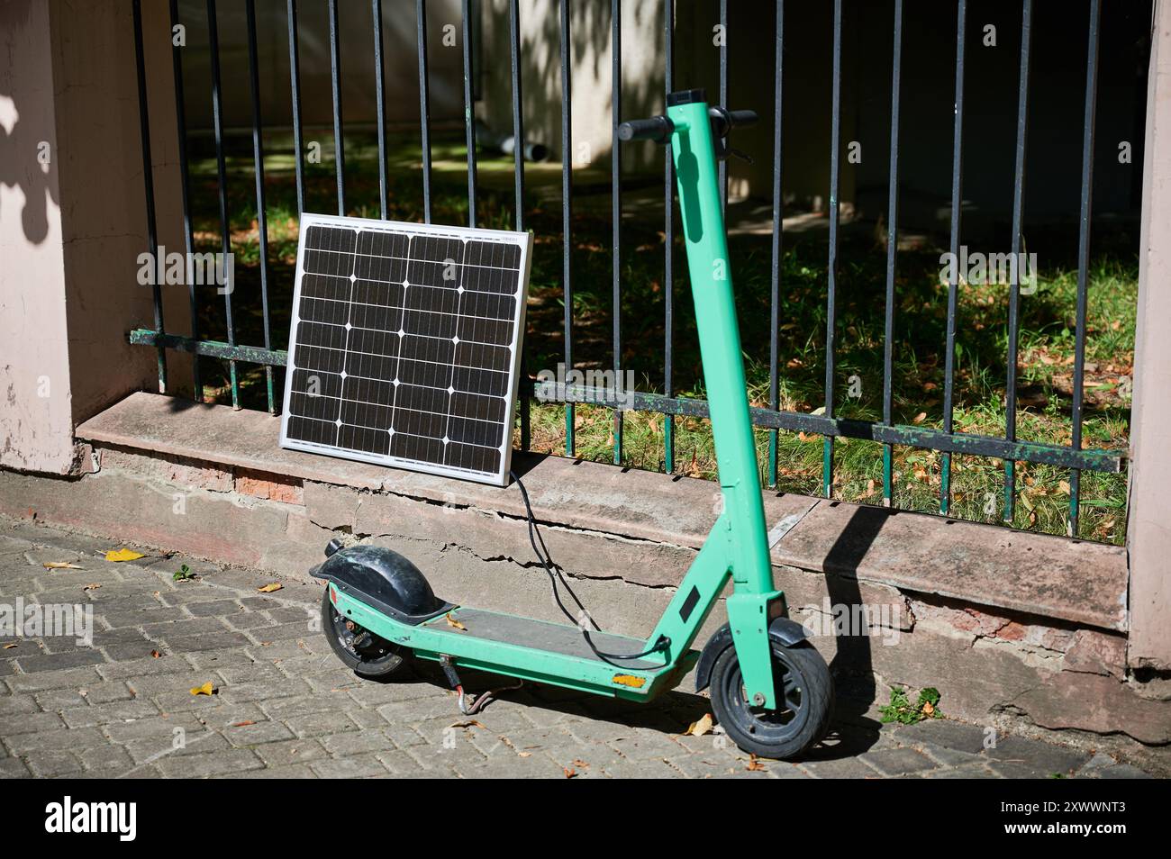 Mint-green electric scooter parked on stone pavement next to solar ...