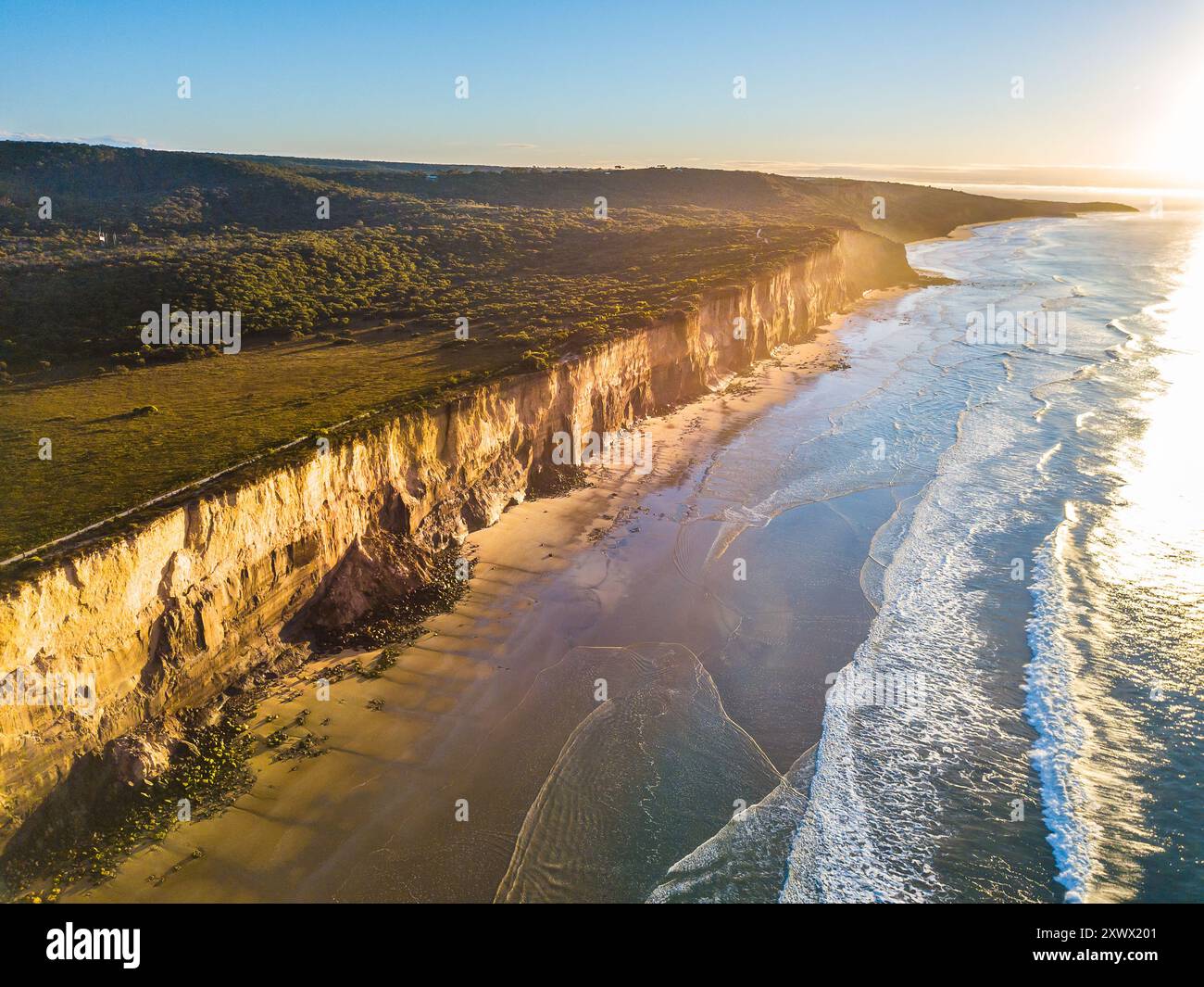 Aerial view of waves crashinf on the base of sea cliffs during sunrise ...