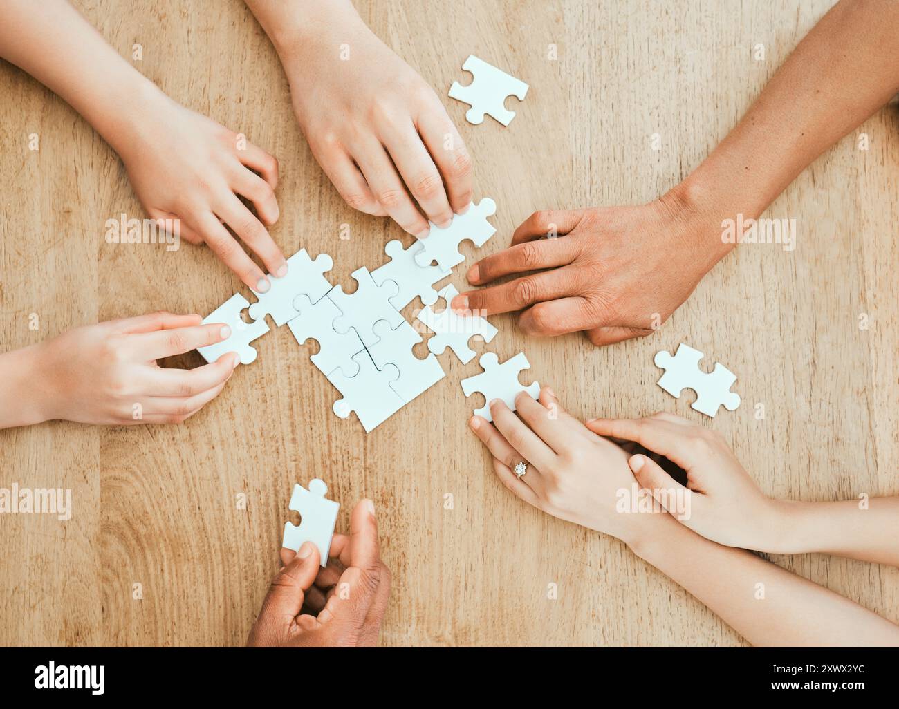 Hands, puzzle and teamwork with group of people at wooden table from ...