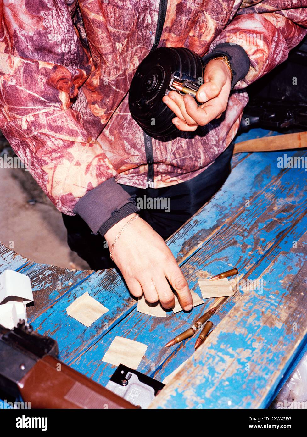 A person is preparing ammunition and handling a magazine on a rustic ...