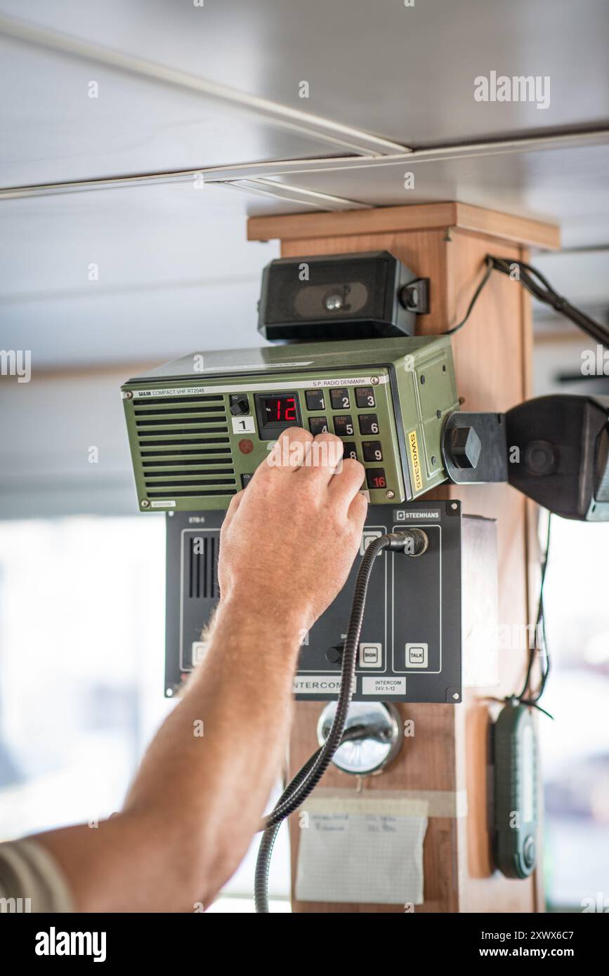 Close-up of a man's hand adjusting a radio device on a boat's interior ...