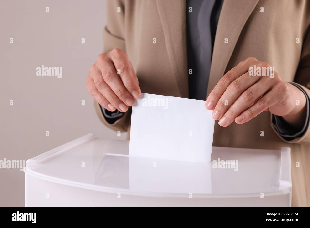 Woman putting her vote into ballot box against grey background, closeup ...