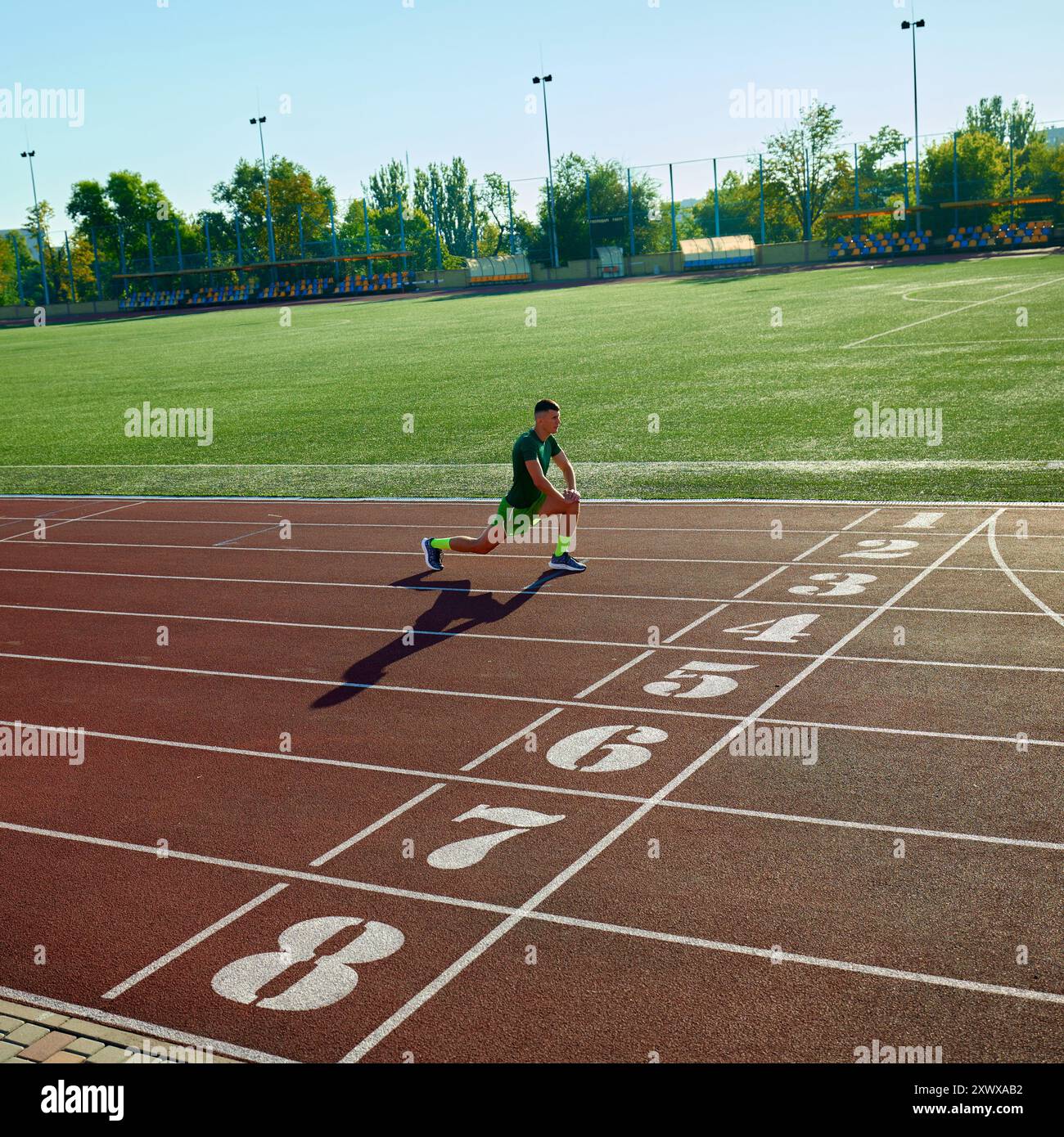 Sprinter, athletic man in green gear warms up with lunge at starting ...