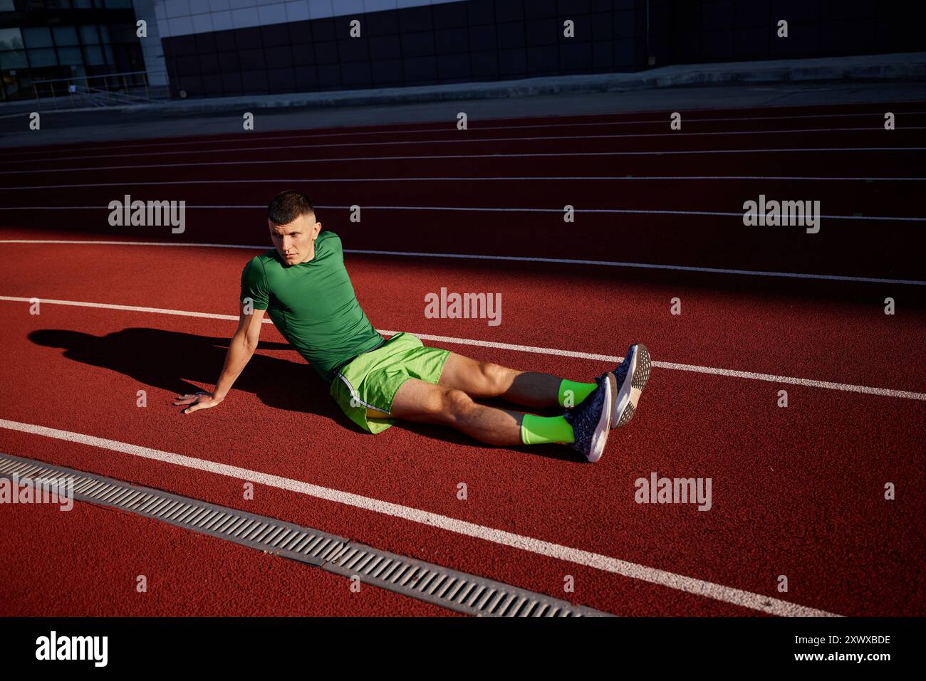 After tough run, athlete sits on the track, deep in thought, his green ...