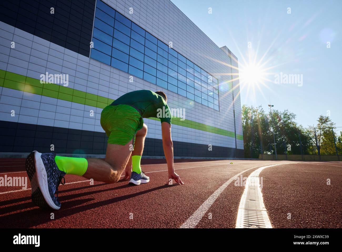 Rear view of young man, athlete in low start position, ready to running ...
