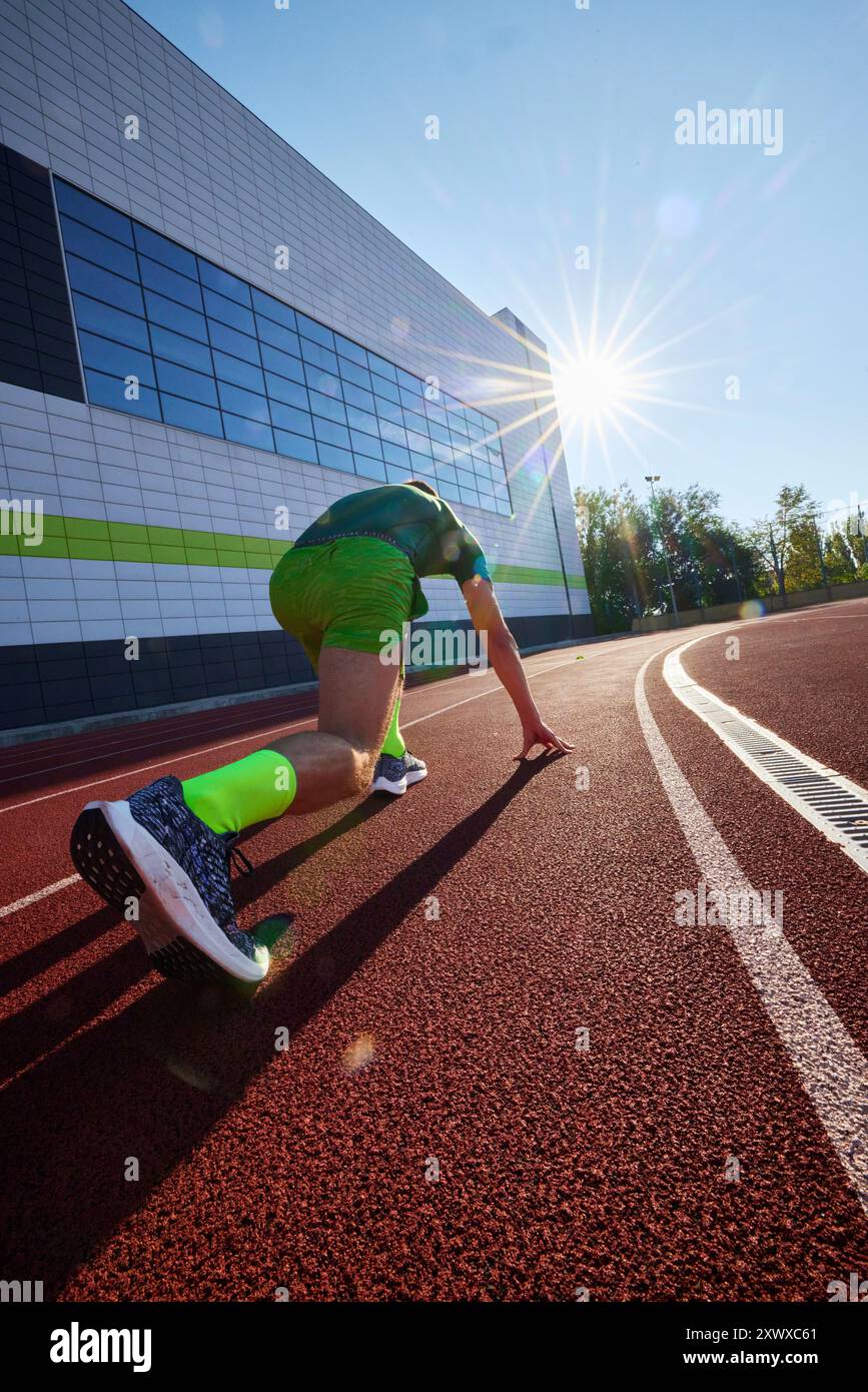 Rear view of young man, athlete in low start position, ready to running ...