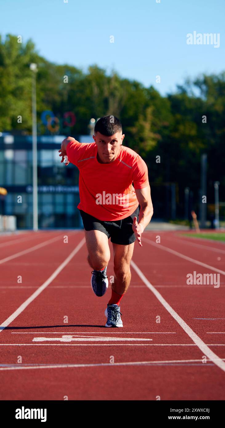 Sprinter in red shirt launches forward on track, eyes locked ahead ...