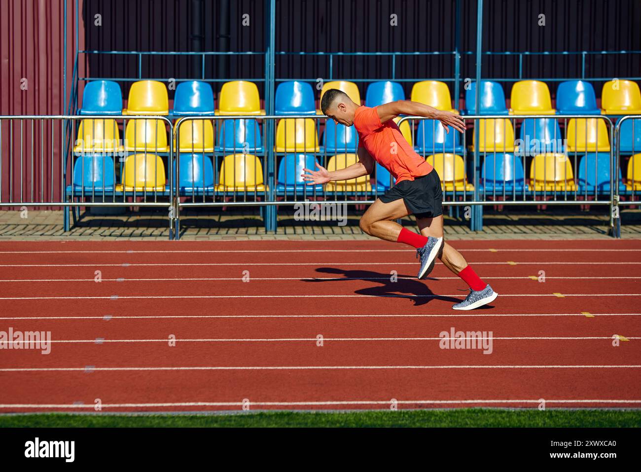 Man, sprinter in bright red shirt propels himself down track, his form ...