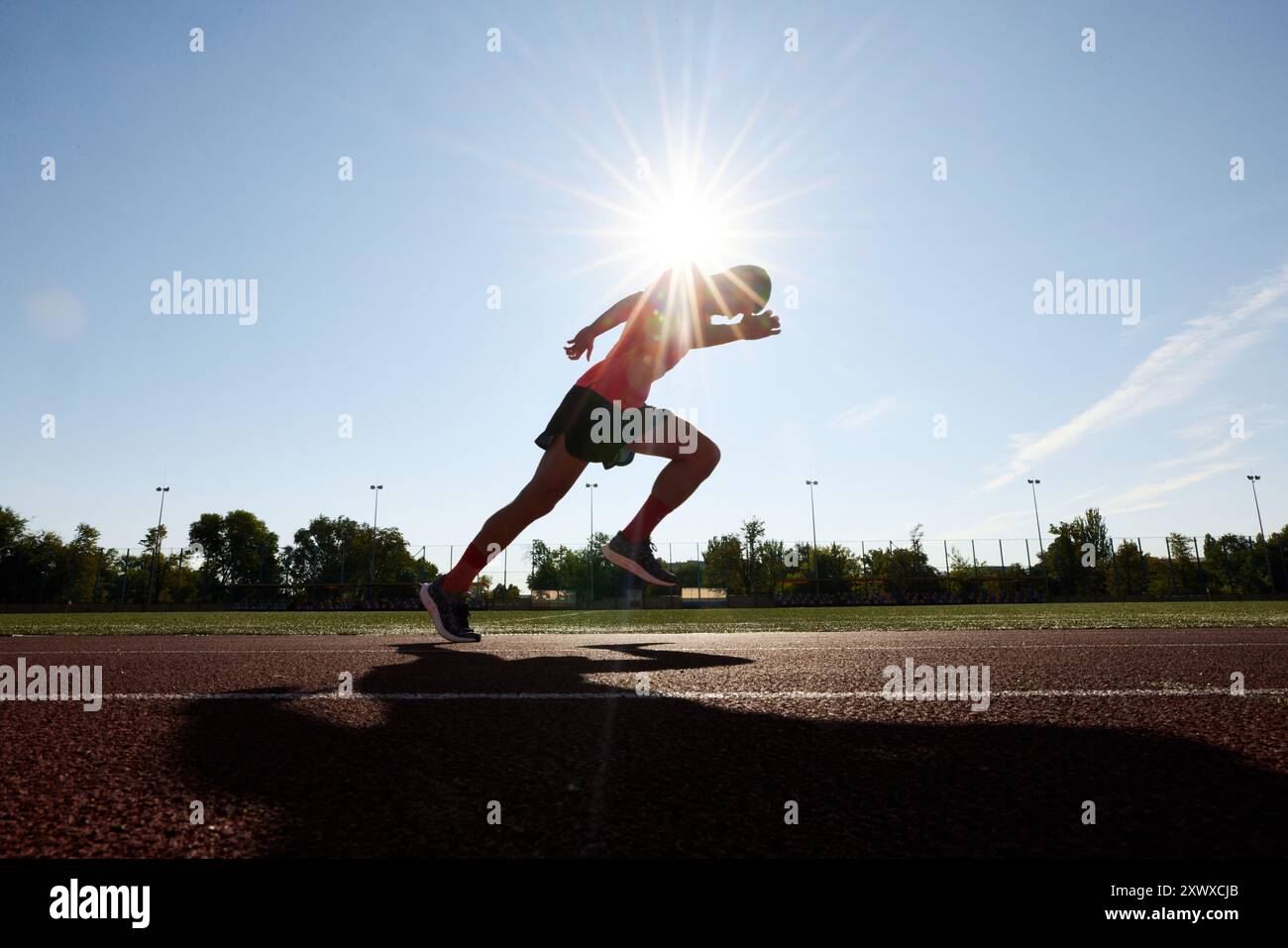 Against blinding sun, athlete in red launches into sprint, his form ...