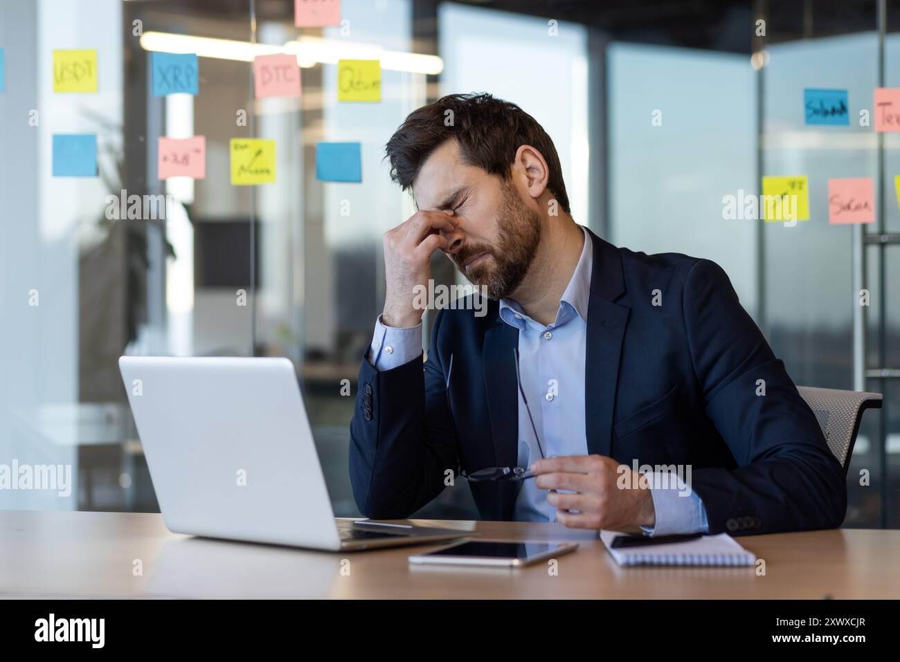 Businessman feeling stressed and overwhelmed, sitting at desk holding ...