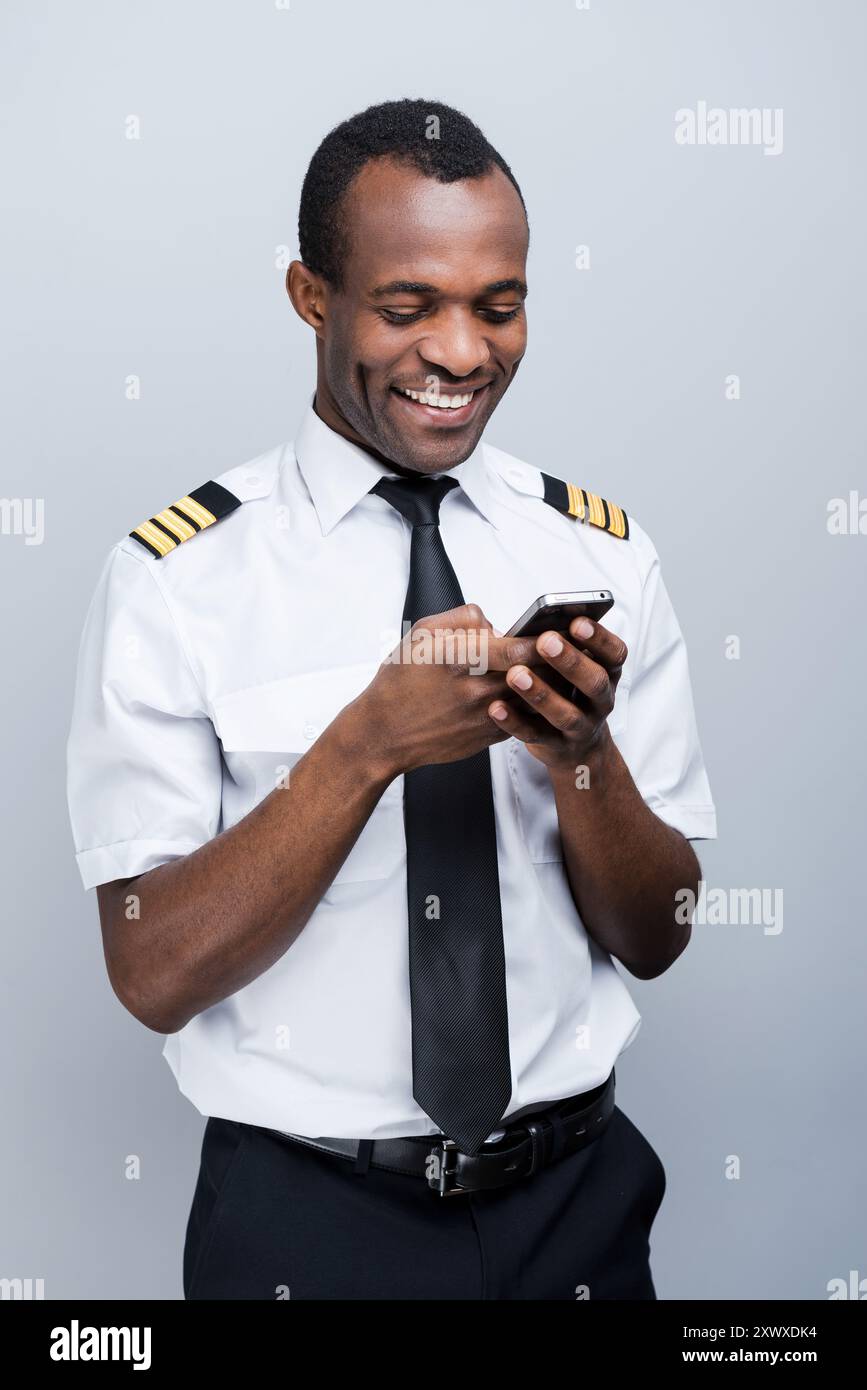 Messages after landing. Side view of happy African pilot in uniform ...